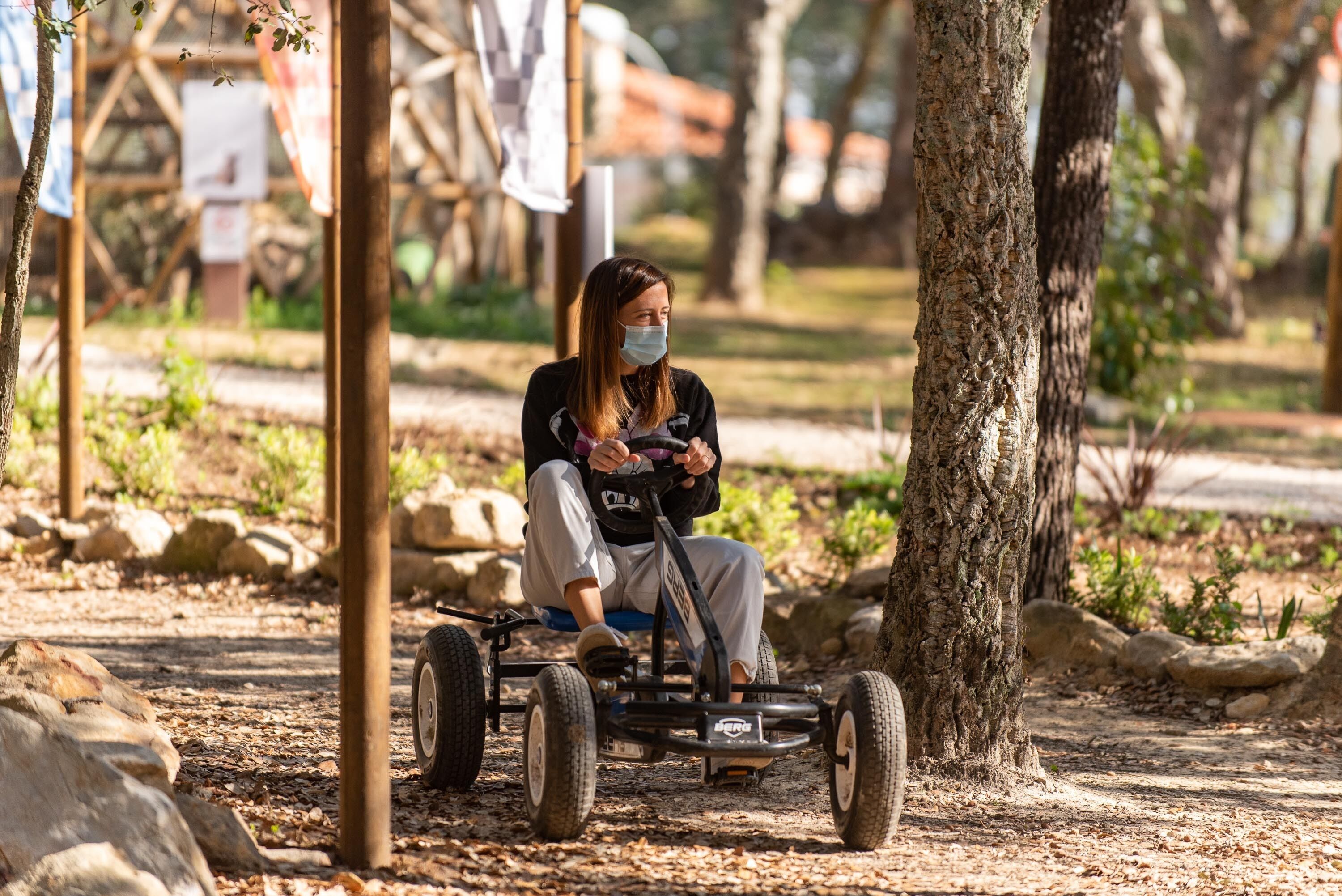 Uma pessoa conduz um veículo de três rodas em um parque arborizado, com árvores e pedras.