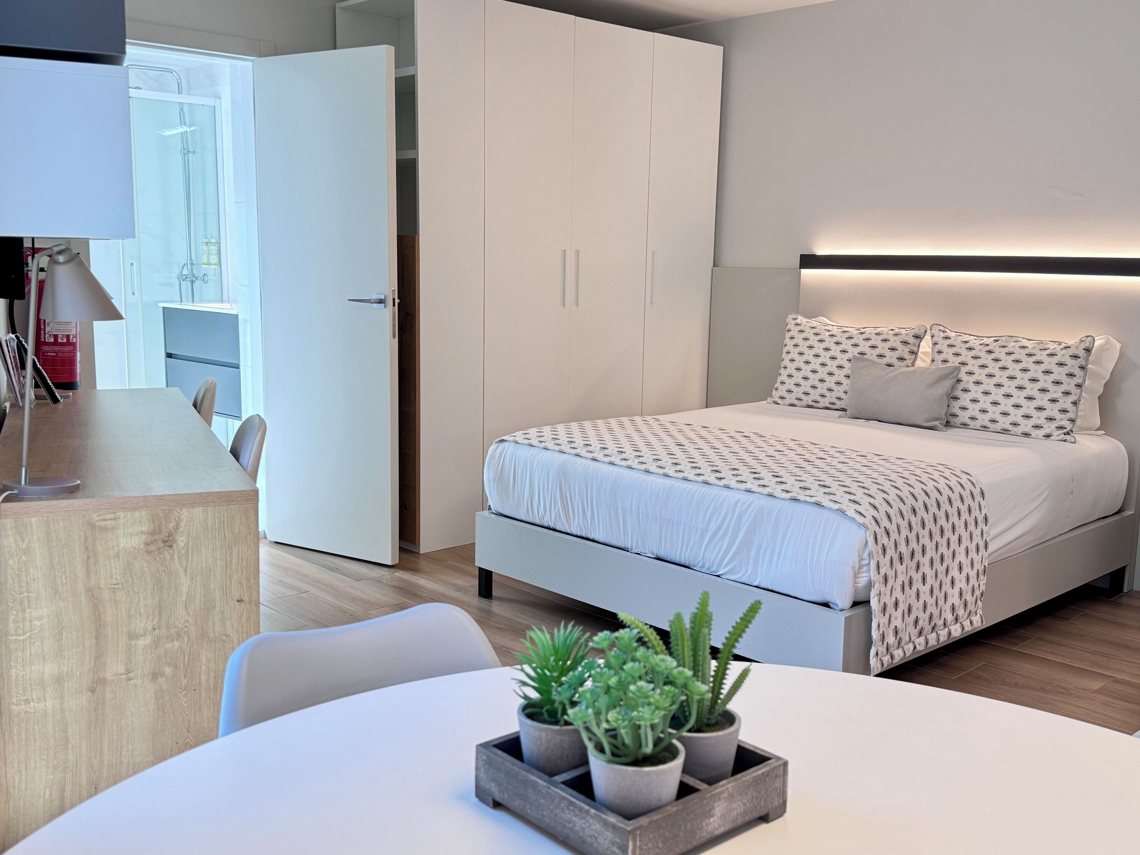 Um quarto moderno com cama, mesas de cabeceira, escrivaninha e uma planta em vaso.