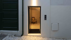 Uma entrada moderna com porta de vidro, uma cadeira no interior e uma luminária acima.
