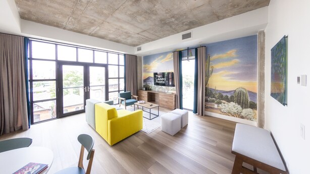 Uma sala de estar ampla com um sofá amarelo, uma mesa de centro de madeira e um mural retratando uma paisagem desértica.
