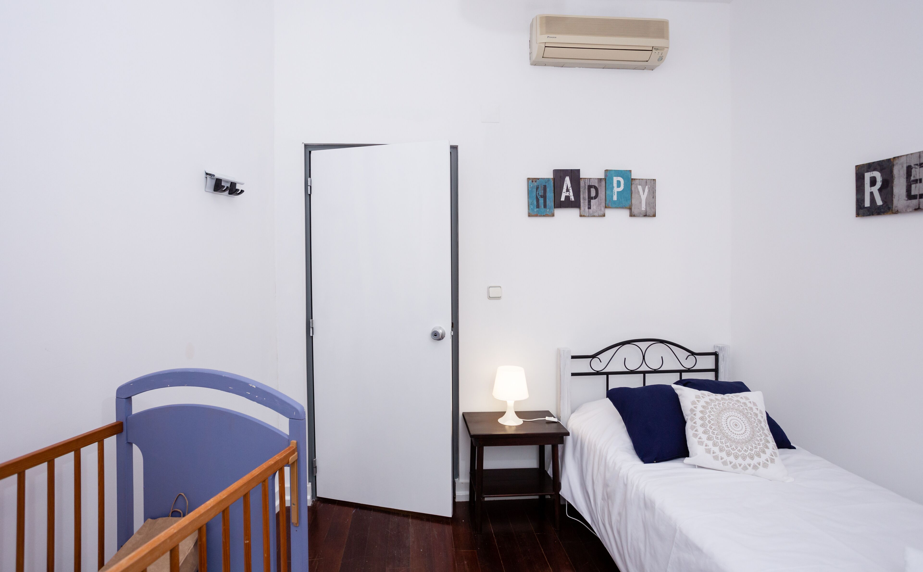 Quarto com cama, mesa de cabeceira, luminária, cadeira e porta.