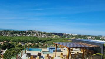 Terraço no telhado com piscina, área de estar ao ar livre e vista para uma cidade costeira.