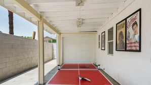 Mesa de pingue-pongue sob uma cobertura, com uma porta de garagem branca ao fundo.