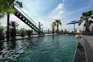 Piscina no terraço com água cristalina, rodeada por vasos de plantas e palmeiras.