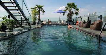 Piscina no terraço com água cristalina, rodeada por espreguiçadeiras e plantas em vasos.