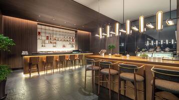 Uma área de bar moderna com balcão de madeira, banquetas, iluminação pendente e uma parede espelhada refletindo o bar.