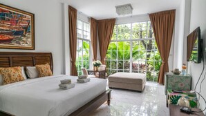Quarto espaçoso com uma cama grande, um espaço de estar e vista para vegetação exuberante através de amplas janelas.