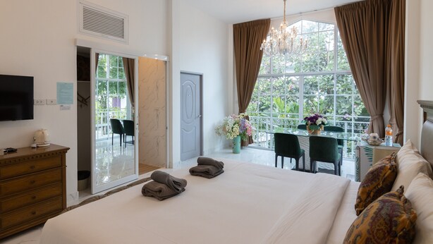 Quarto de hotel com uma cama grande, uma mesa com cadeiras, um candelabro e vista para o verde pela janela.