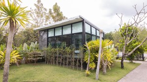 Um edifício moderno com grandes janelas de vidro, rodeado por um jardim bem cuidado com diversas plantas e árvores.