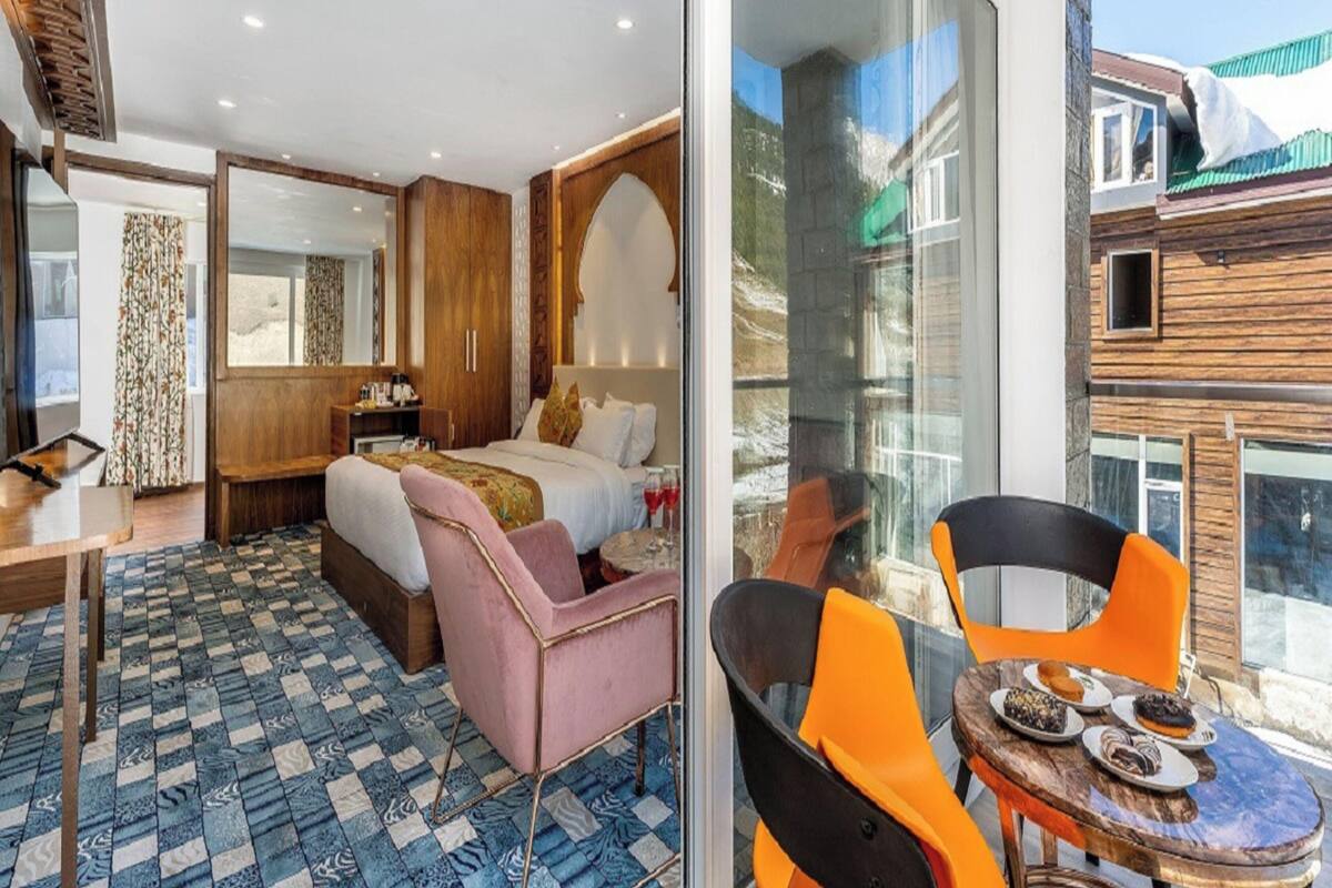 Quarto de hotel moderno com uma cama grande, área de estar com sofá e cadeiras, mesa de jantar com pratos e varanda com vista.