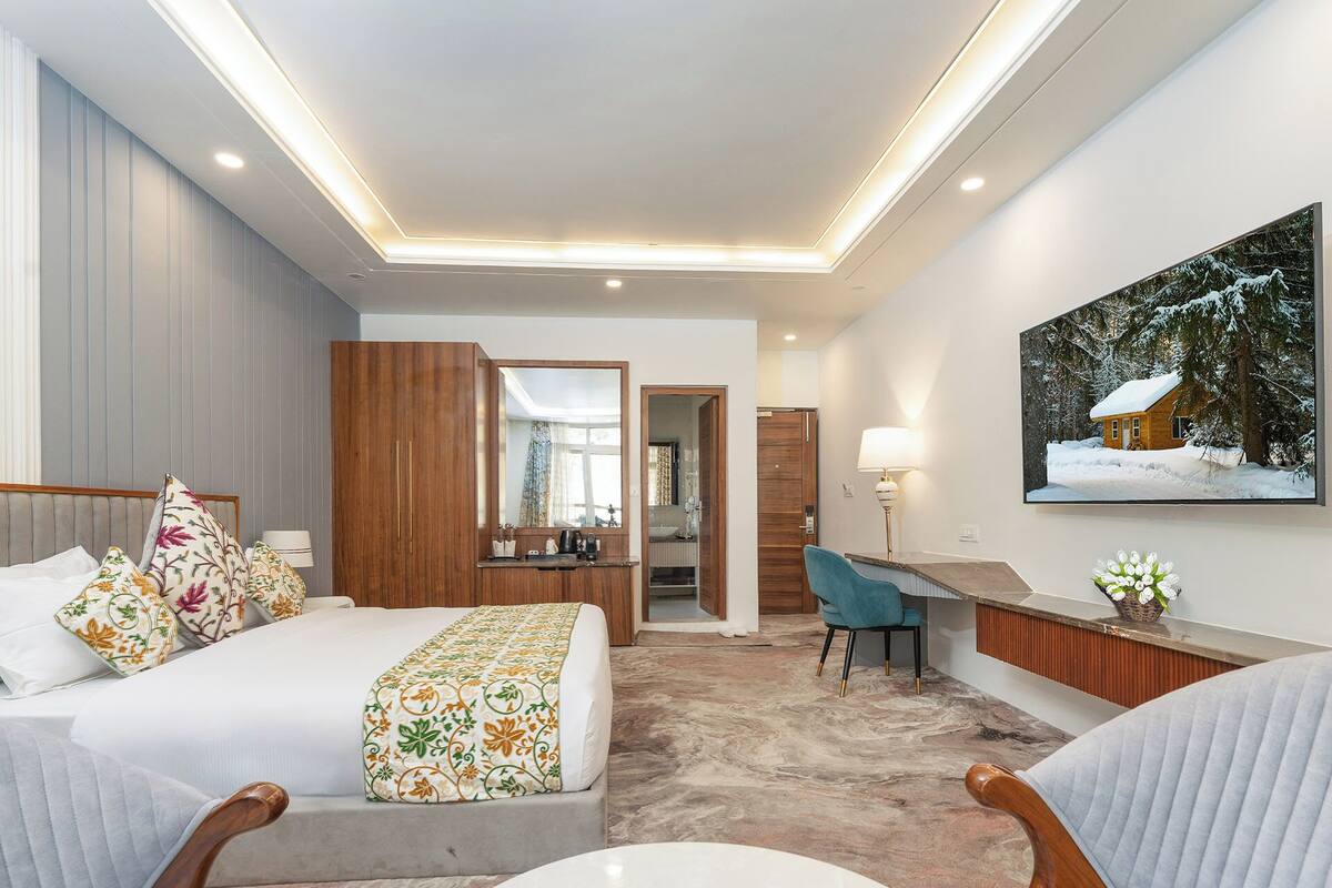 Quarto de hotel com uma cama, uma escrivaninha, uma cadeira, um espelho e um quadro de uma casa nevada.