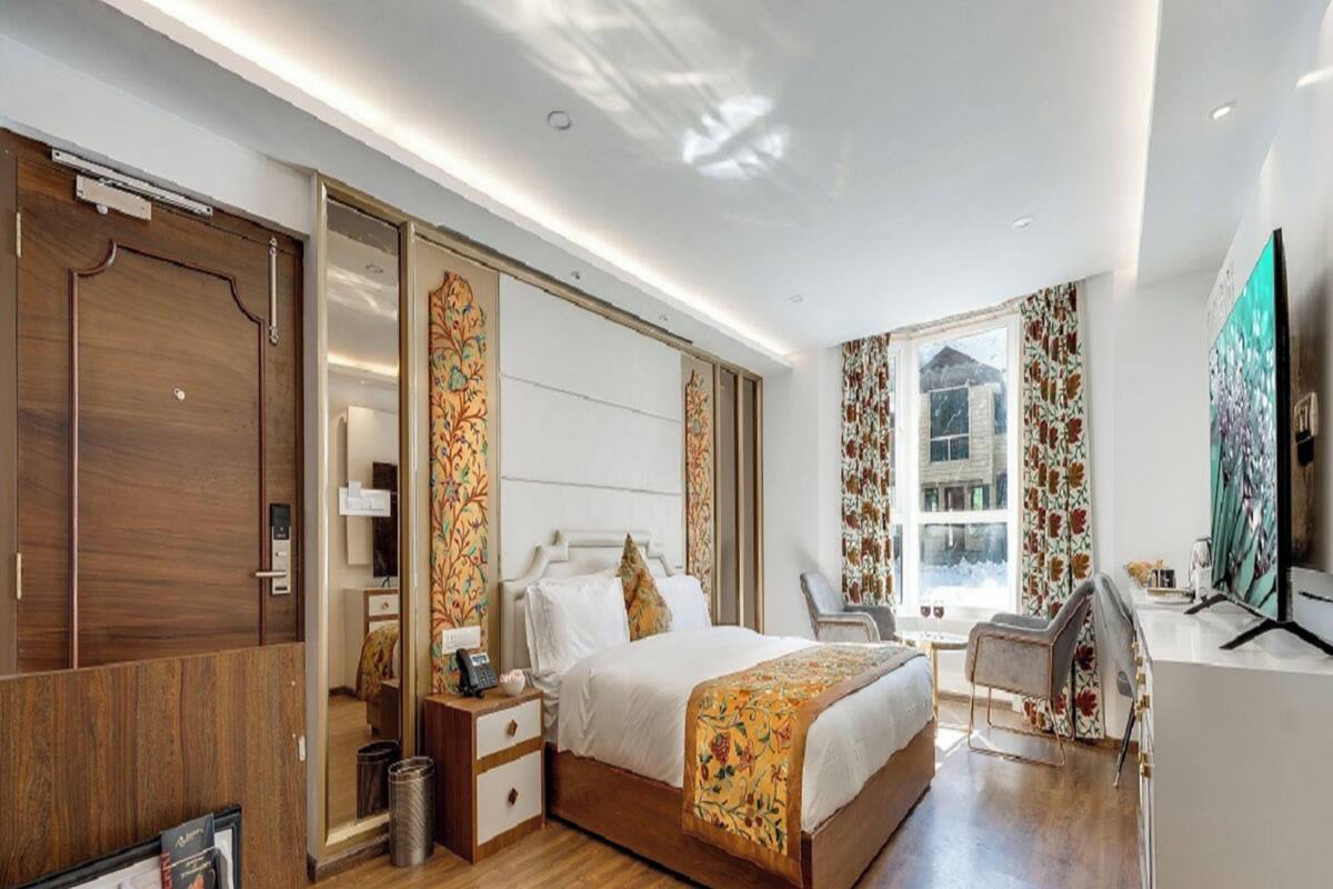 Quarto de hotel moderno com uma cama grande, uma escrivaninha, uma cadeira, uma televisão e um guarda-roupa.
