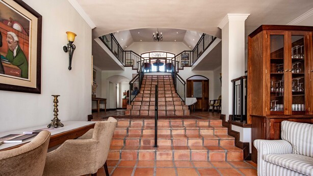 Uma sala de estar espaçosa com uma escadaria imponente, um lustre e um armário tradicional.