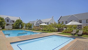 Uma área de piscina com duas piscinas, espreguiçadeiras e guarda-sóis.