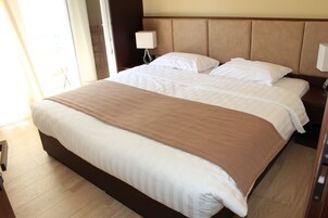 Quarto de hotel com uma cama grande, uma mesa de cabeceira com abajur e vista para o exterior.