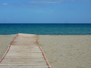 Um calçadão de madeira que leva a uma praia com águas azul-claras.