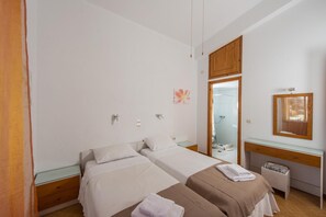 Quarto com duas camas, guarda-roupa de madeira, cabine de chuveiro em vidro e escrivaninha de madeira com espelho.