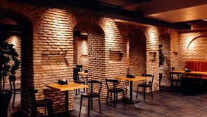 Um restaurante com paredes de tijolo, mesas de madeira e cadeiras pretas.