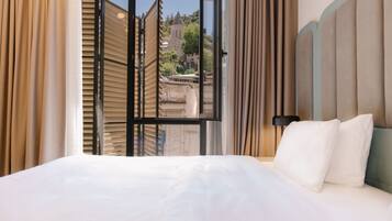 Quarto de hotel com uma cama grande, vista pela janela aberta e cabeceira moderna.