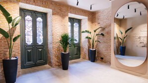 Um corredor com paredes de tijolo, janelas amplas e plantas em vasos.