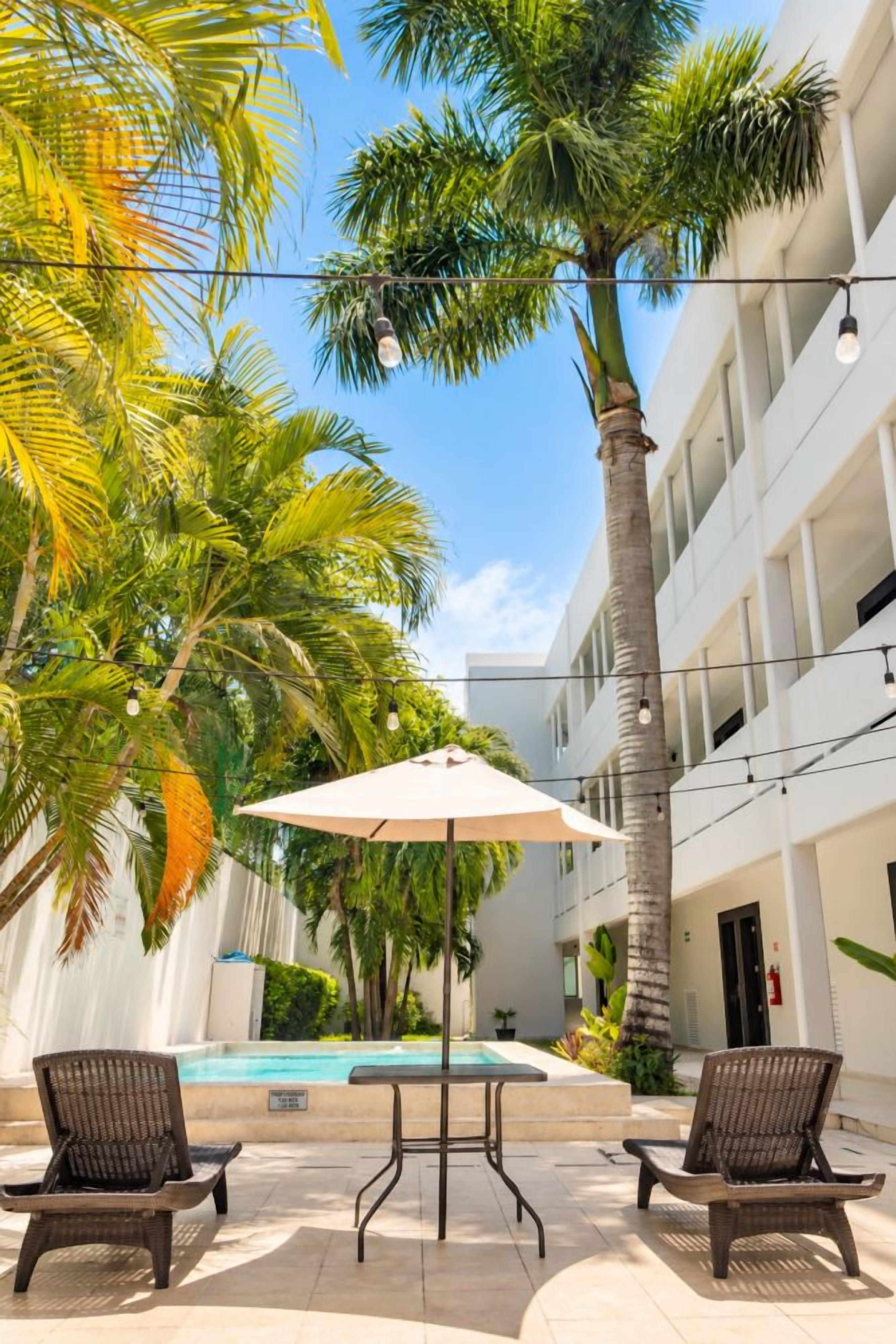 Área de piscina com espreguiçadeiras, uma mesa e um guarda-sol.