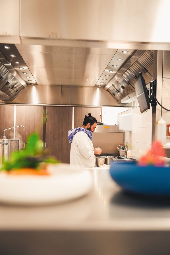 Cozinha moderna com eletrodomésticos de aço inoxidável, uma pessoa preparando alimento e uma tigela azul no balcão.