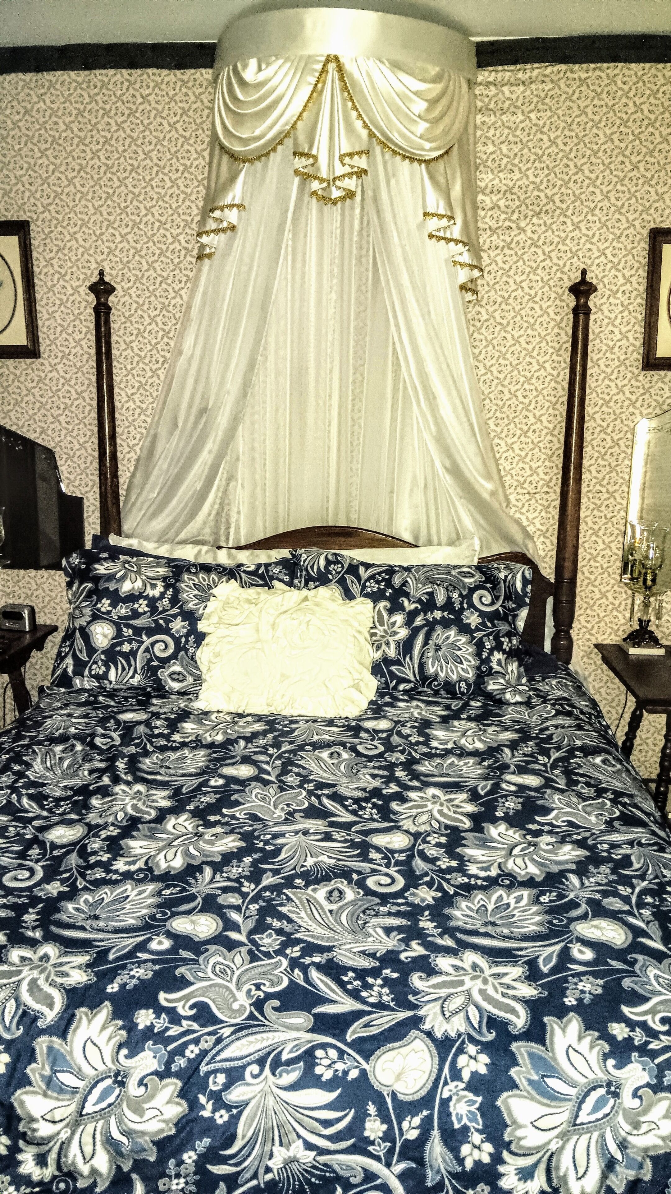 Uma cama com dossel, roupa de cama estampada com flores e uma mesa de cabeceira com abajur.
