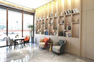 Um lobby moderno com piso de mármore, área de estar com cadeiras e sofás, e uma estante com objetos decorativos.