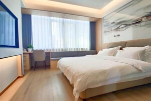 Quarto de hotel moderno com cama grande, escrivaninha e janela com cortinas.