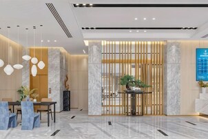 Um lobby moderno com balcão de recepção, área de estar e uma planta decorativa.