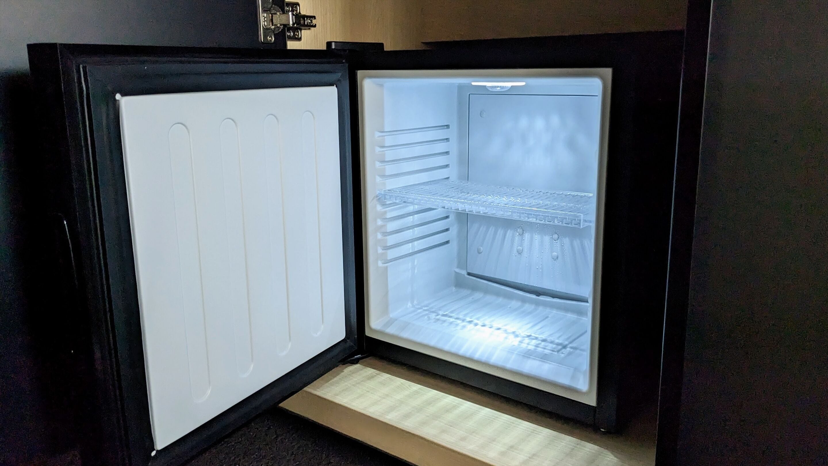 Um pequeno frigorífico aberto com porta transparente, mostrando suas prateleiras e compartimentos internos.