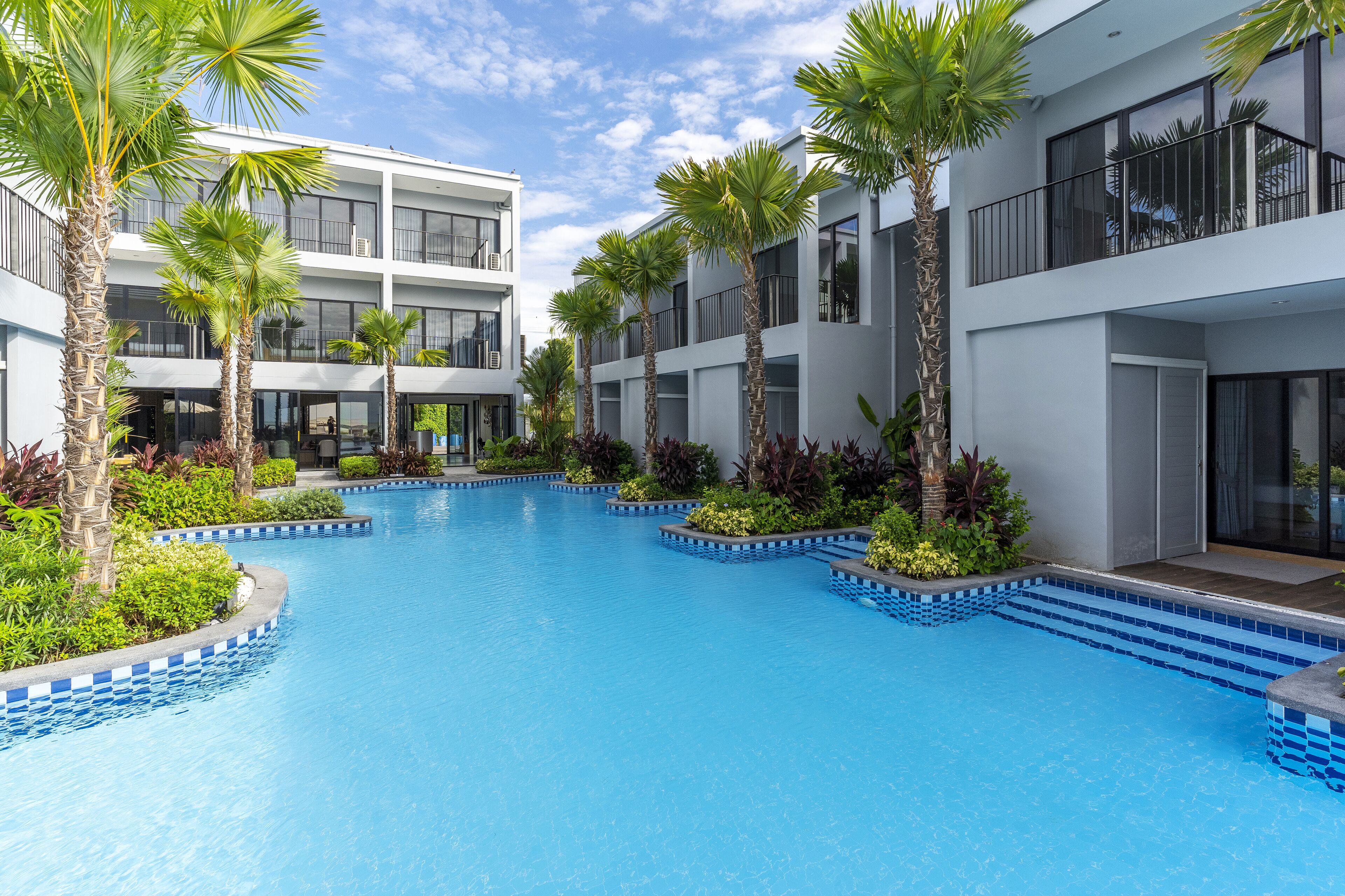 Um hotel moderno com piscina central cercada por palmeiras e plantas.
