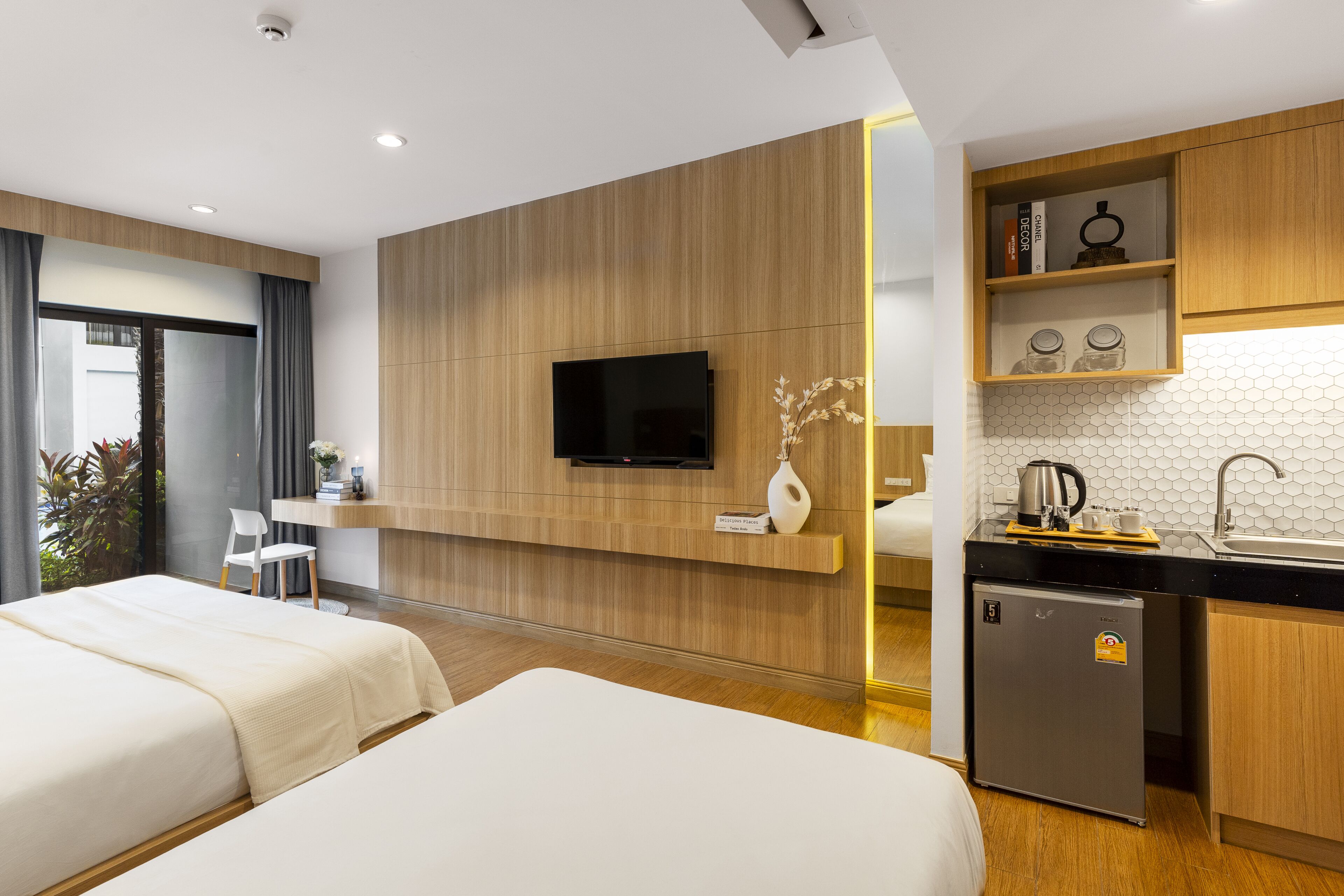 Quarto de hotel moderno com duas camas, televisão, pequena cozinha e vista para o exterior.