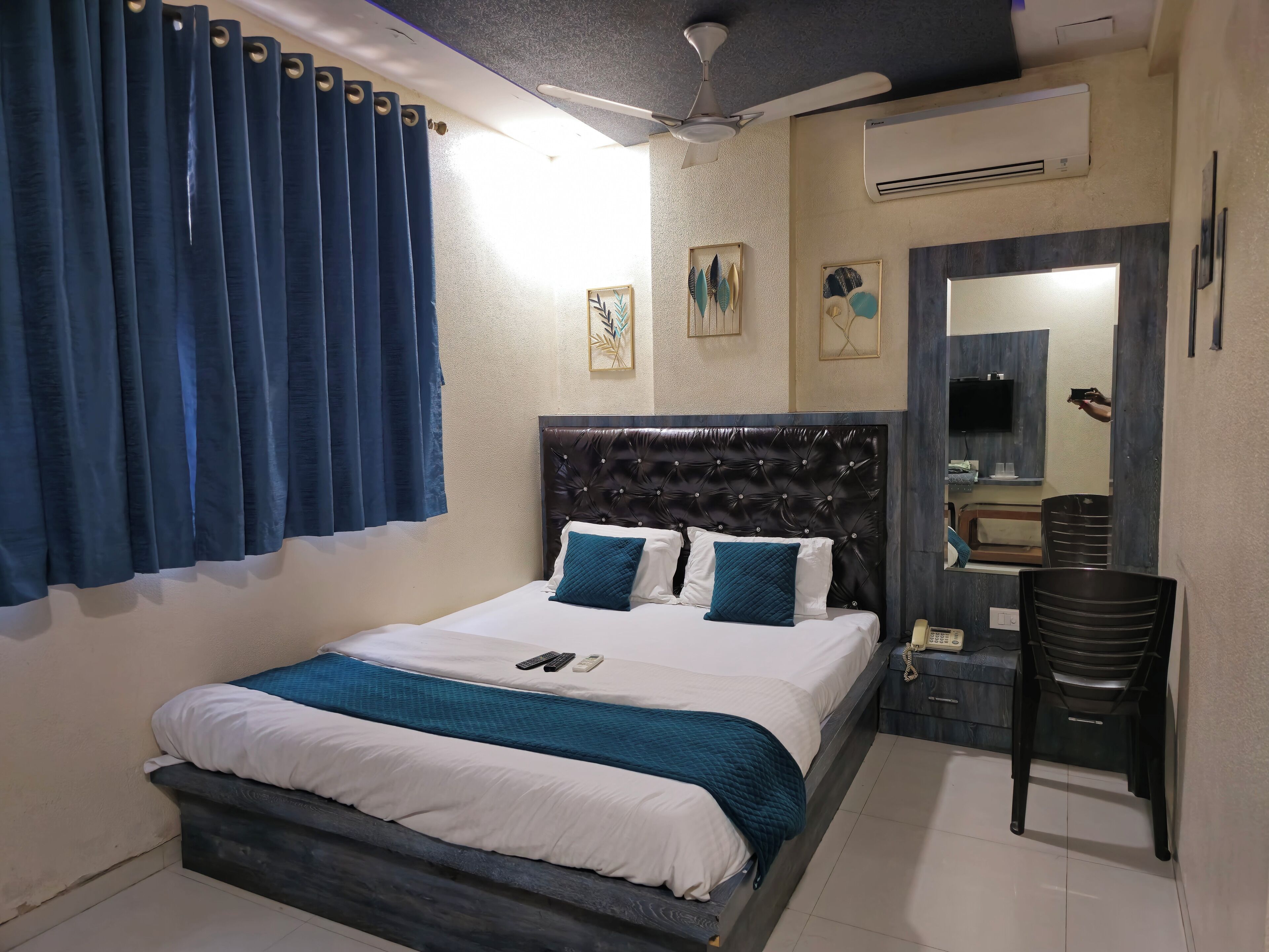 Quarto com cama, mesa de cabeceira com telefone, espelho e cadeira.