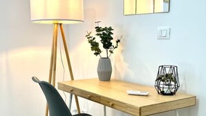 Uma mesa moderna com cadeira, uma luminária de chão, um vaso com plantas e um espelho decorativo na parede.