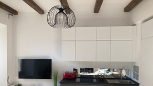 Uma cozinha moderna com armários brancos, forno embutido, torradeira vermelha e uma TV de tela plana na parede.