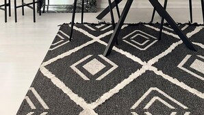 Uma área de refeições com espelho emoldurado em mármore, uma mesa redonda com cadeiras pretas e um tapete estampado.