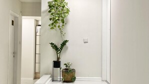 Uma escadaria com degraus brancos conduz a um patamar. Há duas plantas em vasos no patamar: uma em um vaso preto e outra em uma cesta de palha.