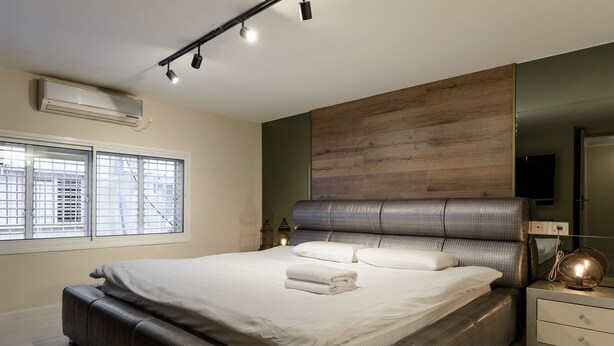 Quarto moderno com cama grande, mesas de cabeceira, ar condicionado fixado na parede e janela com persianas.