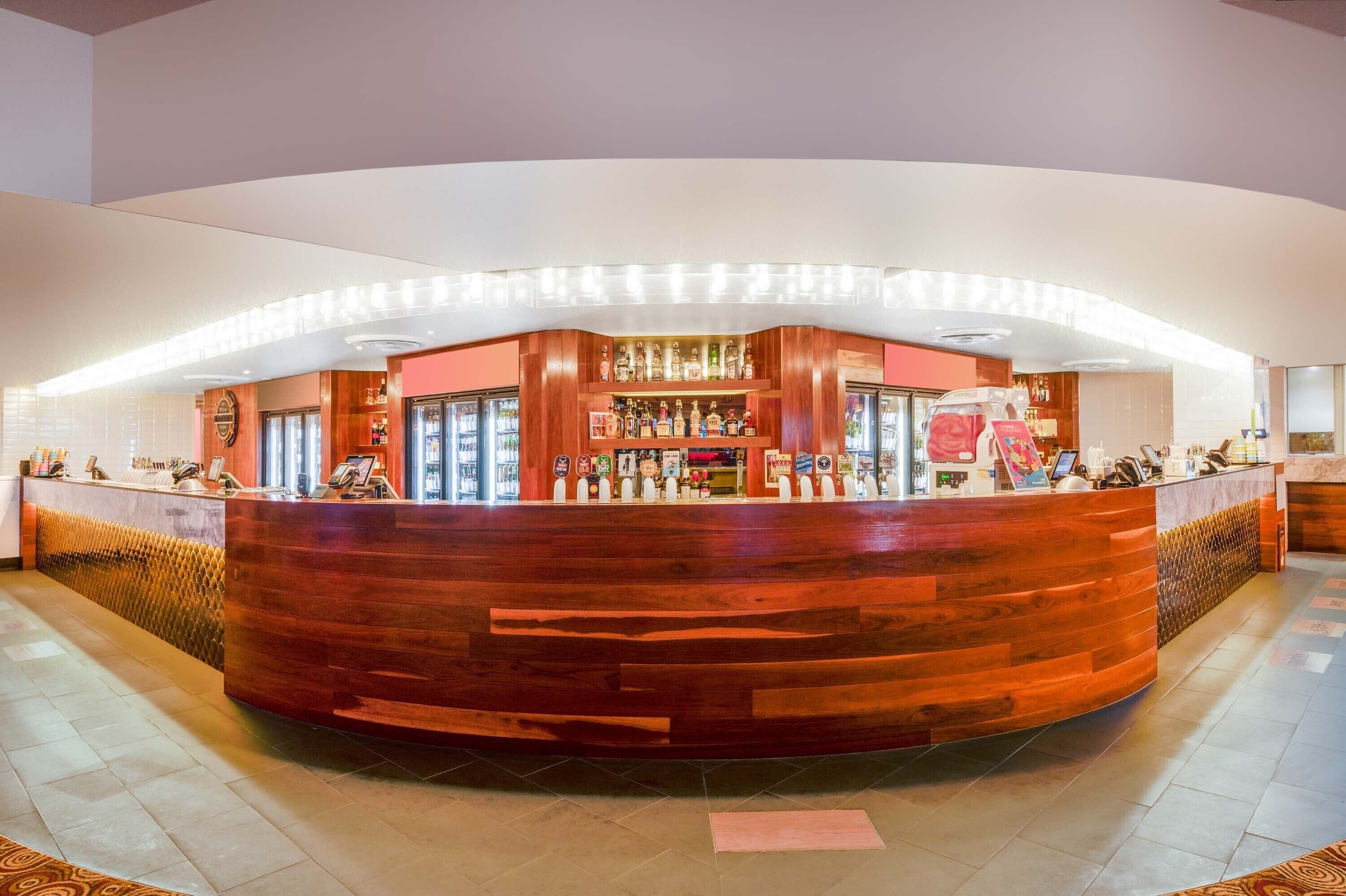 Uma área de recepção com balcão de madeira curvo, bar com diversas garrafas de bebidas e design de interiores moderno.
