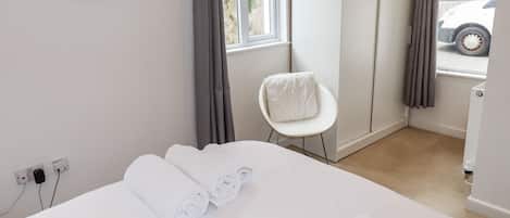 Quarto de hotel com cama, uma cadeira, guarda-roupa e janela com cortinas.