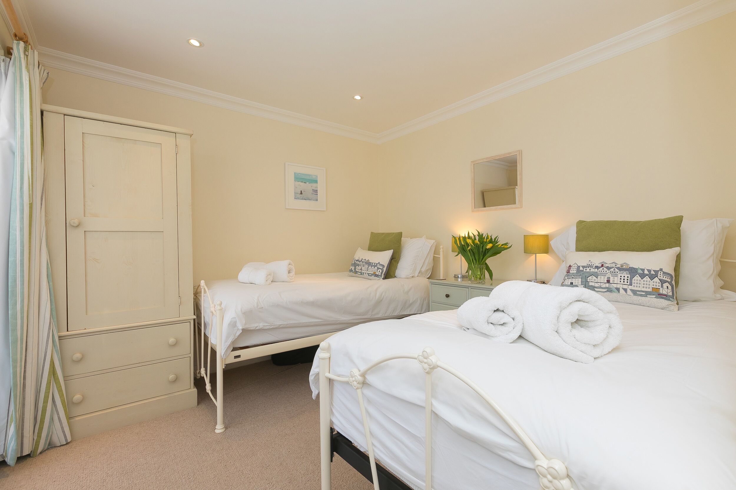 Quarto de hotel com duas camas de solteiro, um guarda-roupa, mesa de cabeceira com abajur e um quadro na parede.
