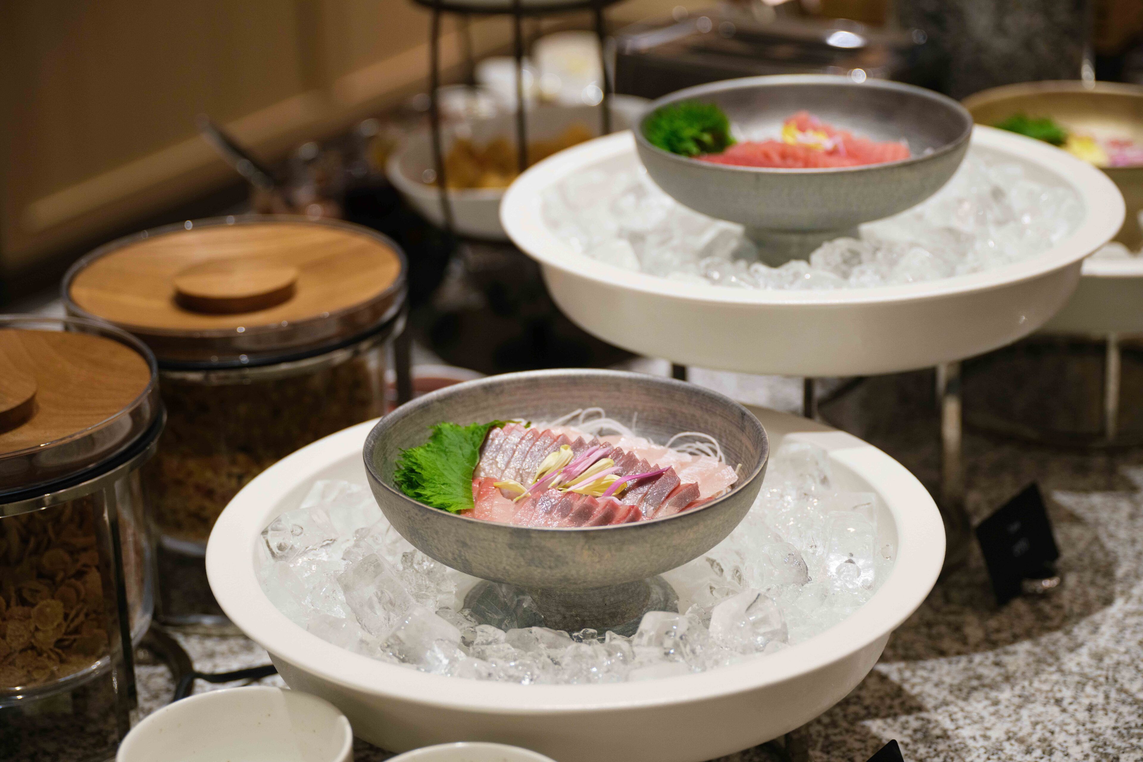 Buffet com diversos pratos servidos em cubos de gelo, incluindo uma tigela de carne fatiada e legumes.