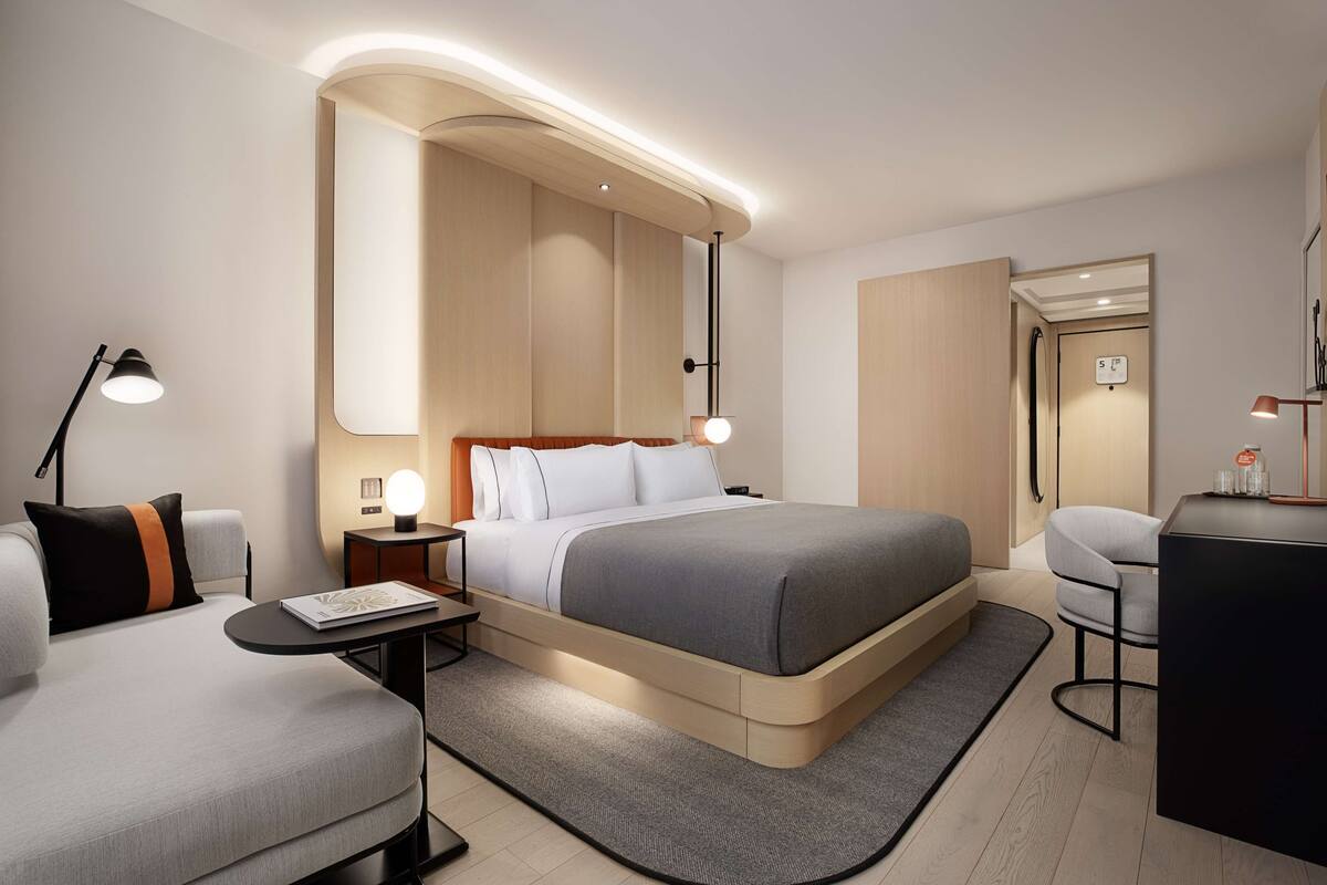 Quarto de hotel moderno com cama, mesa de cabeceira, abajur e escrivaninha com cadeira.