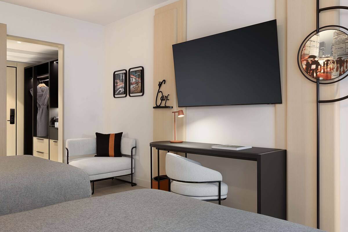 Quarto de hotel moderno com cama, escrivaninha, cadeira, televisão e espelho.