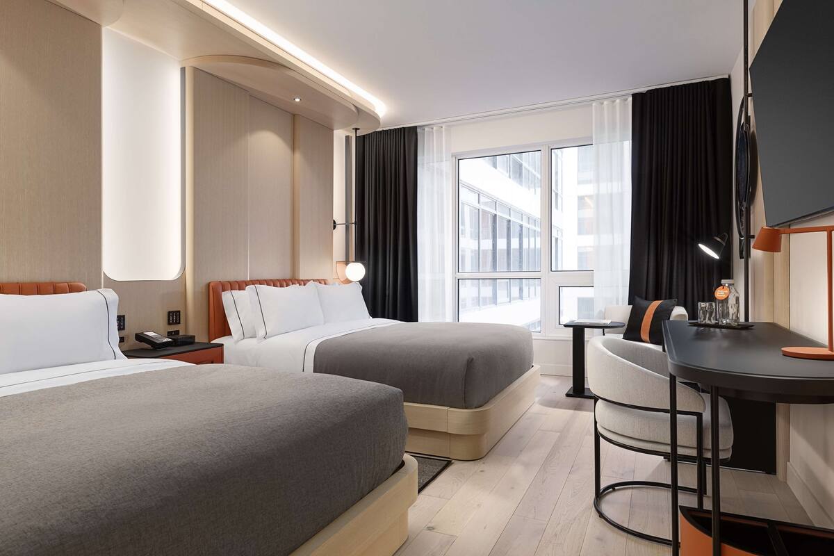 Quarto de hotel com duas camas, uma mesa pequena, uma cadeira e uma televisão.