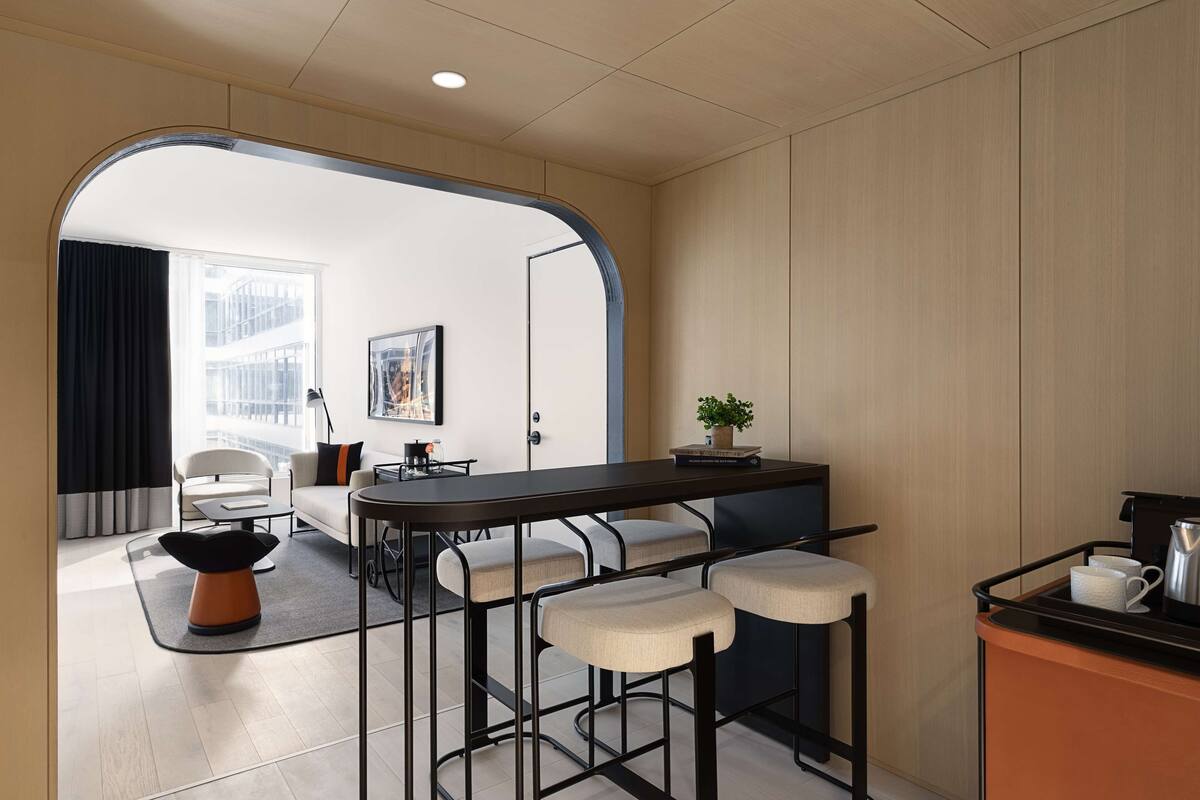 Quarto de hotel moderno com área de bar, assentos e vista da cidade.
