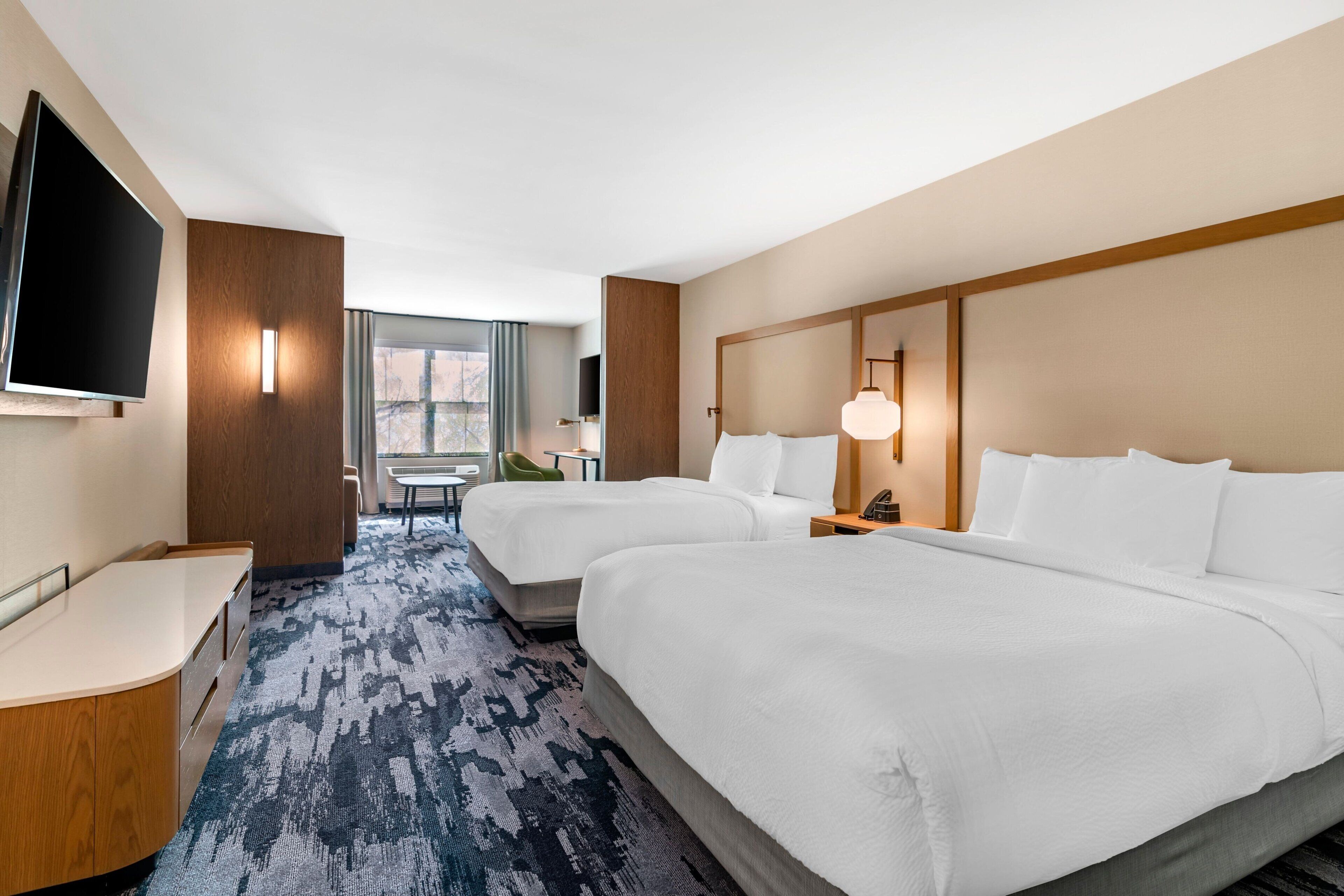 Quarto de hotel com duas camas, uma escrivaninha, televisão de tela plana e uma janela grande.