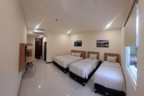 Quarto de hotel com três camas, uma janela e um corredor que leva a outro quarto.