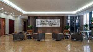 Um lobby moderno com área de estar central, uma grande obra de arte abstrata na parede e uma mesa de recepção à direita.